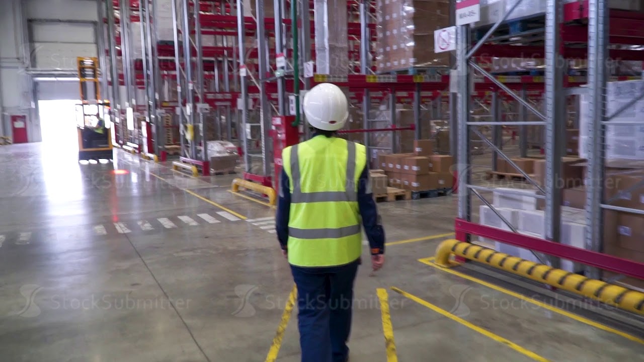 female warehouse worker with helmet and safety vest. Clip. Young female in protective uniform