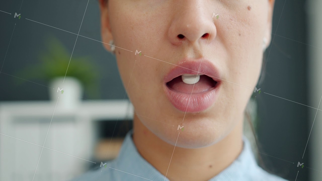 Close-up portrait of unhealthy young woman opening mouth taking pill indoors