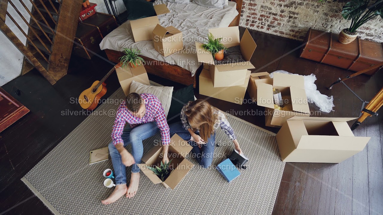 Top view of happy young couple unpacking things, opening box, taking things and talking after moving