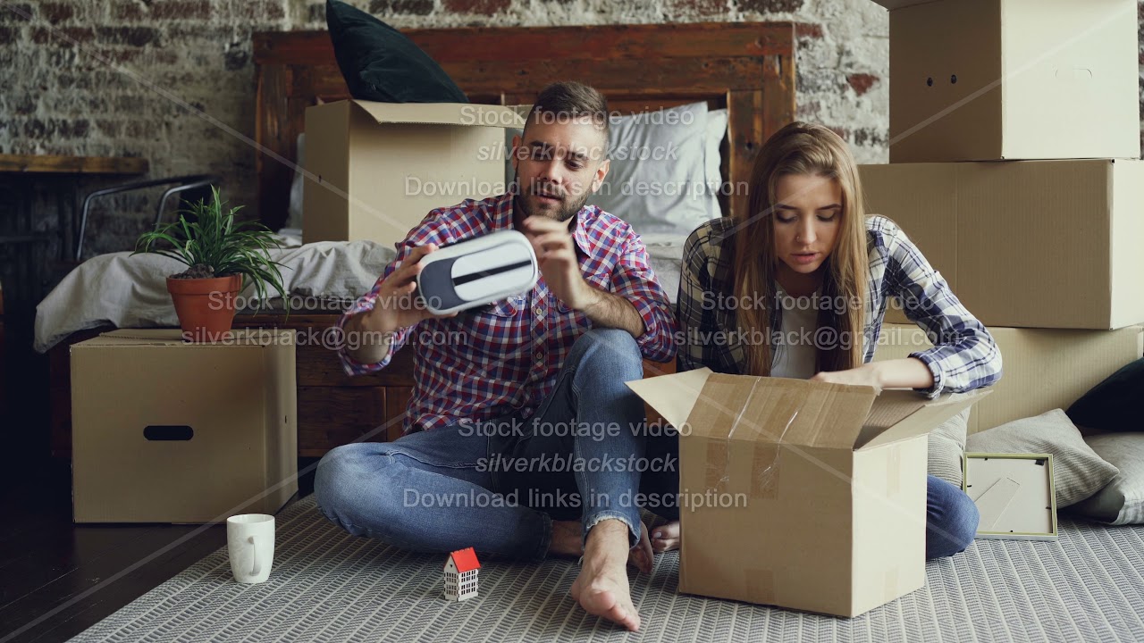 Excited young couple is unpacking things, opening box, taking personal items and talking after