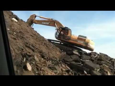 Excavator climbing huge asphalt stockpile (landfill chronic