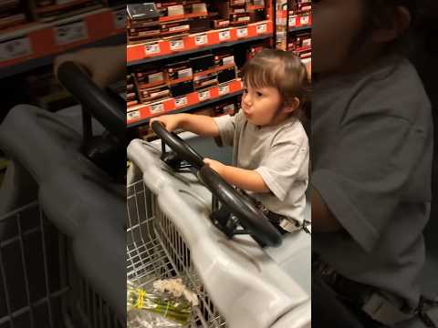 Two year old girl driving through home depot store in mini car shopping cart