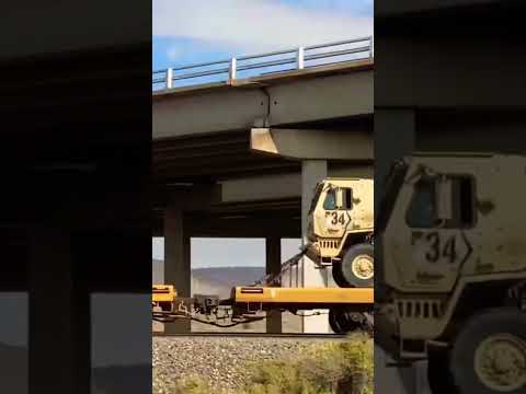 Military Armored Vehicles being transported on Railroad Train passing under Highway Bridge