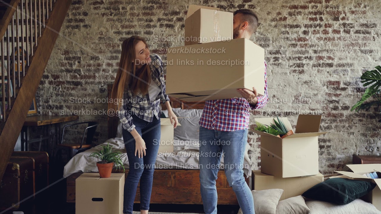 Attractive couple is moving boxes in bedroom in their new home, guy is carrying things while his