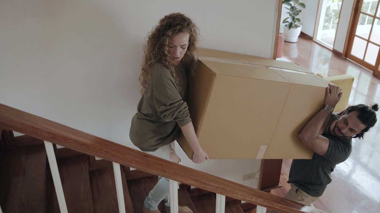 A Couple Carrying Boxes Moving In To Their New Home