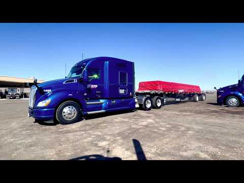 System Transport Flatbed Truck Pulls Out of the Terminal with Tarped Freight, Ready for Delivery!