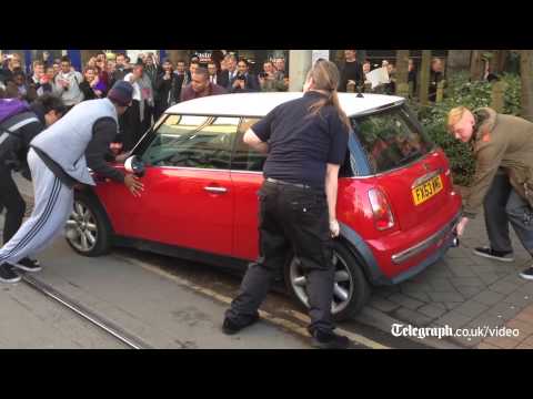 Group of men lift Mini blocking tram in Nottingham