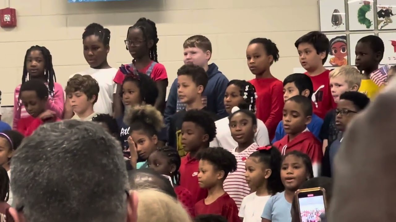 Elementary school kids sing “we are marching for our veterans”.