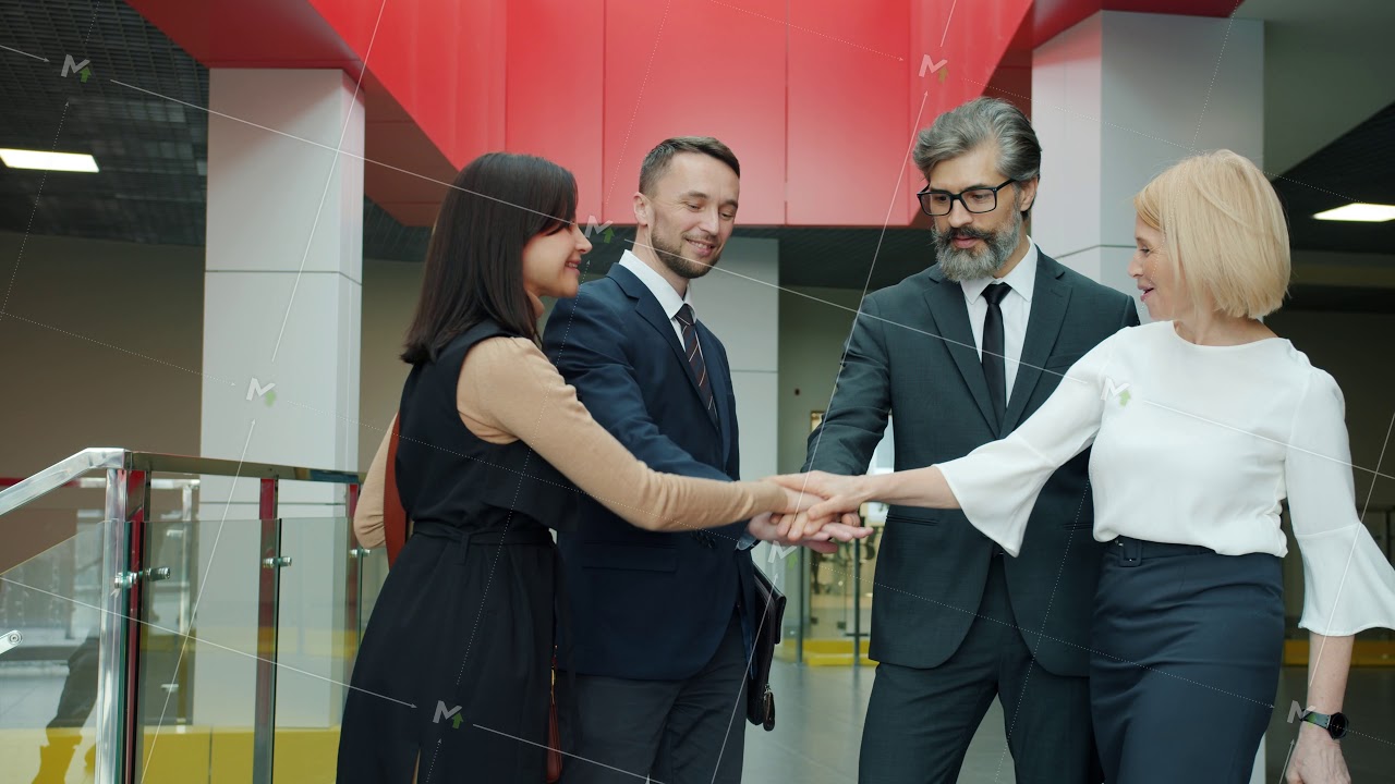 Portrait of business partners joining hands in office center showing thumbs-up